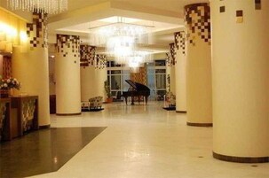 Um hall espaçoso com um piano de cauda, pé-direito alto e pilares decorativos.