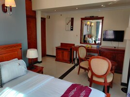 Quarto de hotel com cama, escrivaninha, cadeira, televisão e espelho.