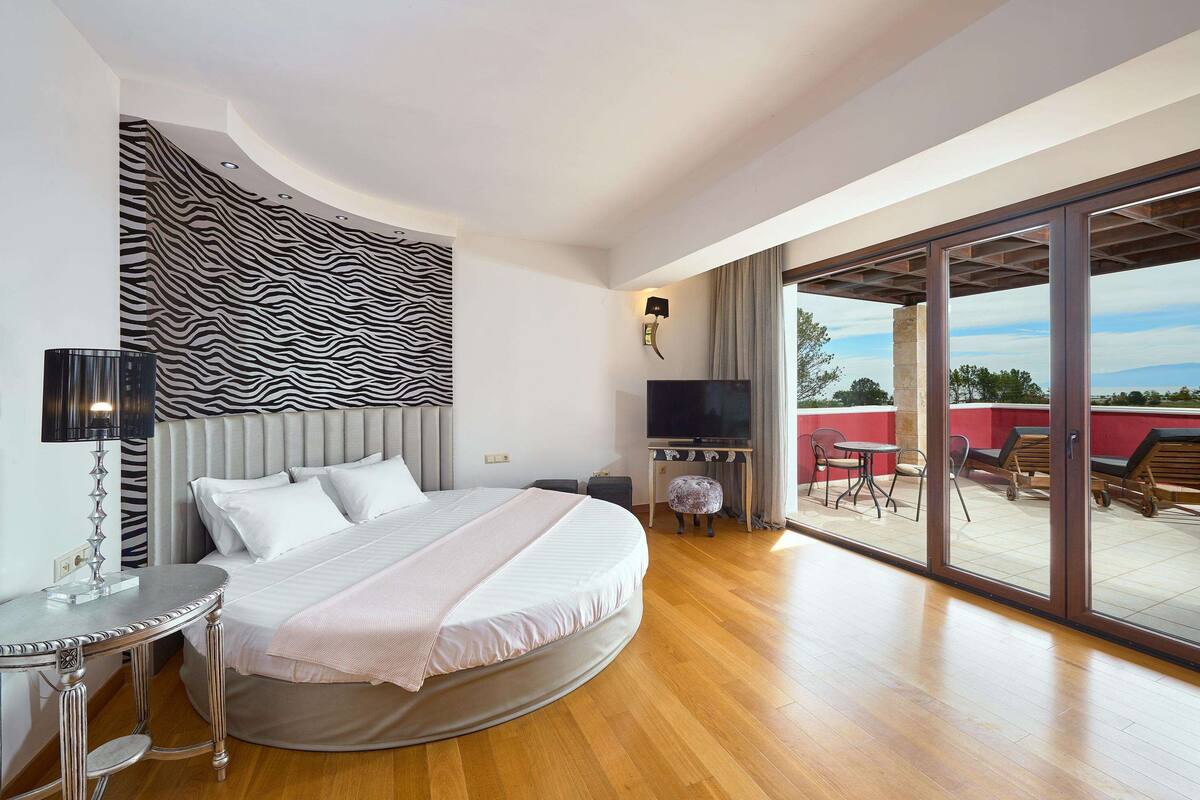 Quarto moderno com cama grande, televisão e varanda com área de estar ao ar livre.
