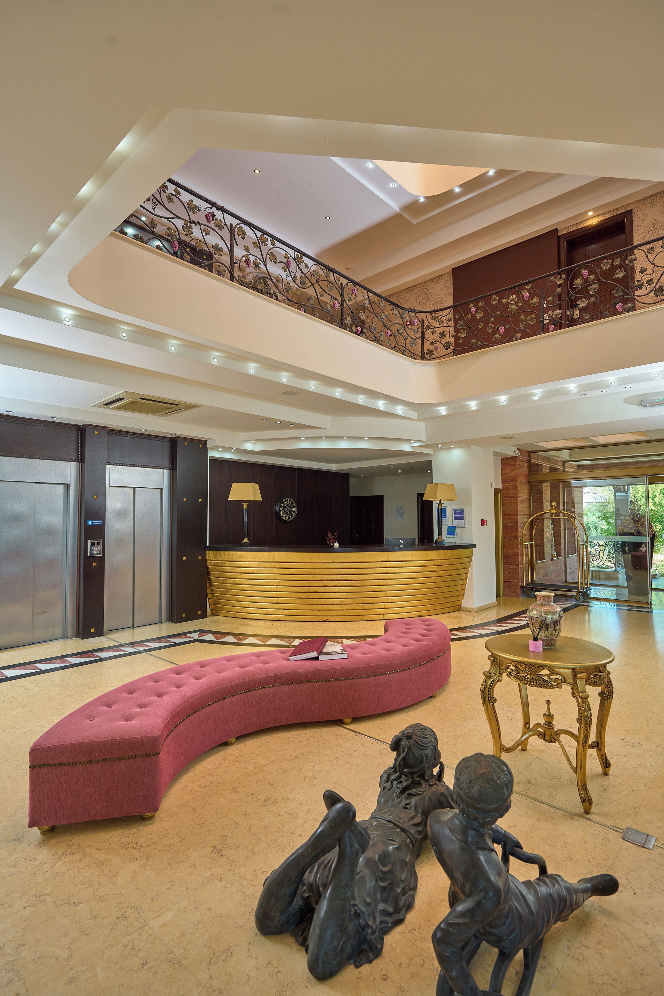 Um saguão de hotel com balcão de recepção, elevadores, uma área de estar vermelha e curva, e uma escultura decorativa.