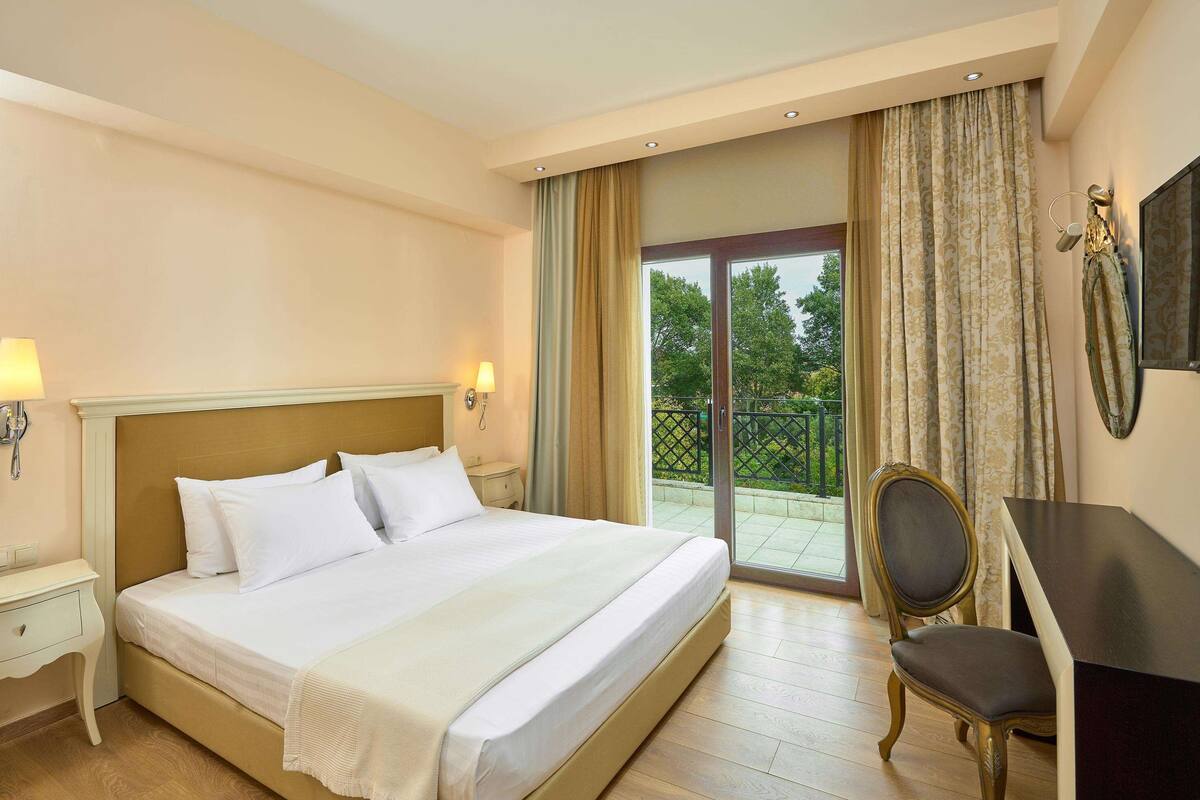 Quarto de hotel com uma cama grande, uma escrivaninha e vista para o exterior através de uma porta de correr.