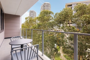 Uma varanda com mesa e cadeiras, com vista para um horizonte urbano com edifícios altos e árvores.