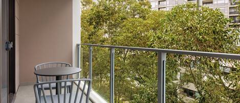 Uma varanda com mesa e cadeiras, com vista para um horizonte urbano repleto de edifícios e árvores.