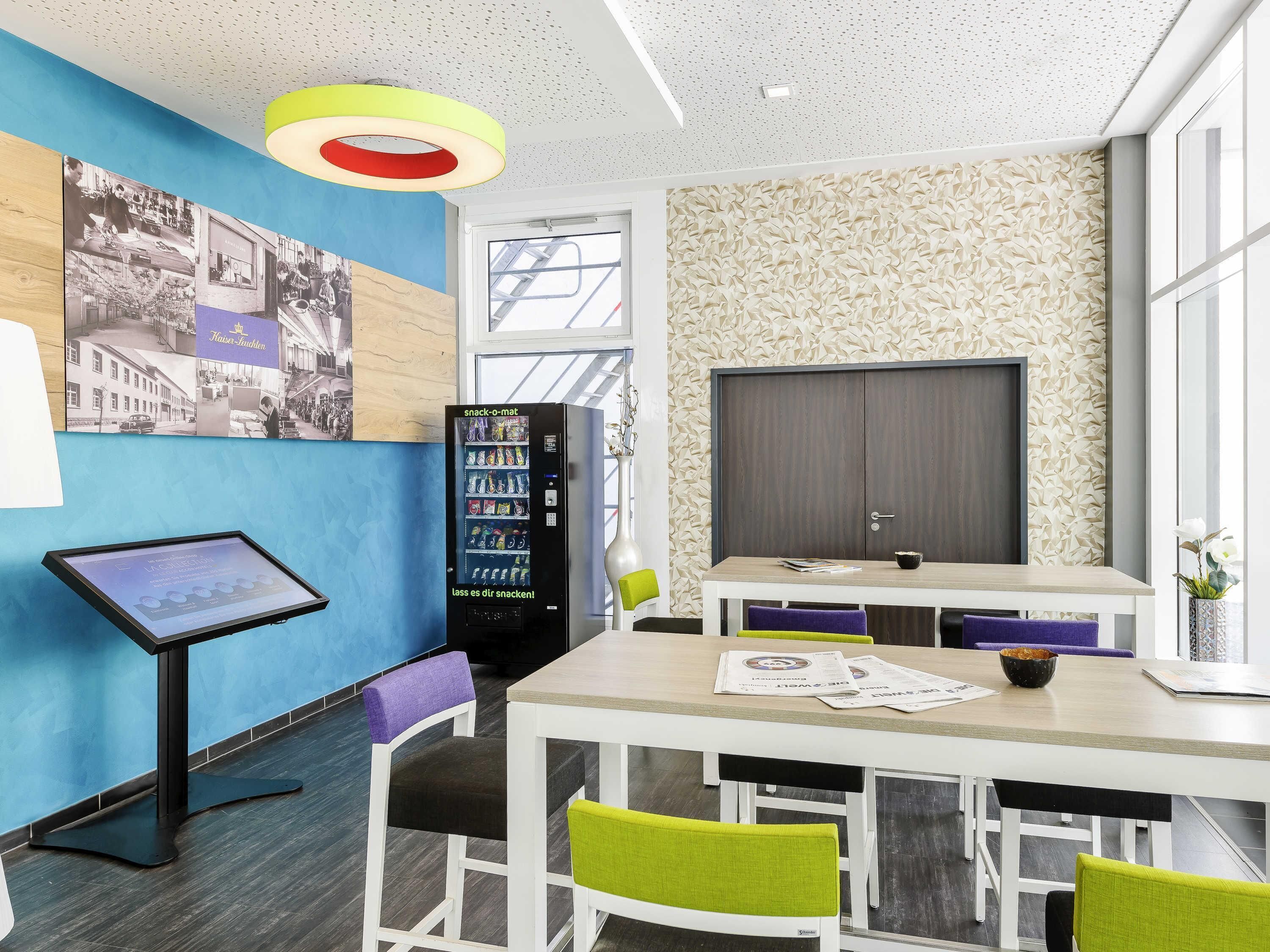 Um interior moderno com uma máquina de venda de lanches, uma mesa com cadeiras e um painel com padrão decorativo.