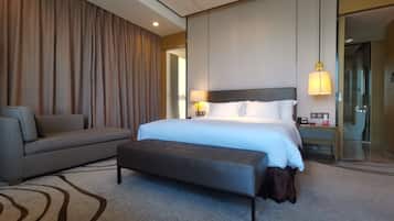 Quarto de hotel moderno com uma cama grande, um sofá, um banco e um espelho.
