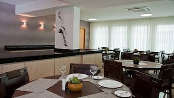 Uma área de refeições moderna com uma mesa redonda central, rodeada por cadeiras, e um balcão comprido com um candeeiro acima.