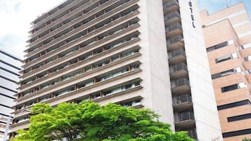 Um hotel moderno com uma placa grande 'HOTEL' na fachada, vários andares e uma placa de estacionamento visível em primeiro plano.