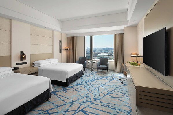 Quarto de hotel com duas camas, televisão, escrivaninha e vista para a cidade.