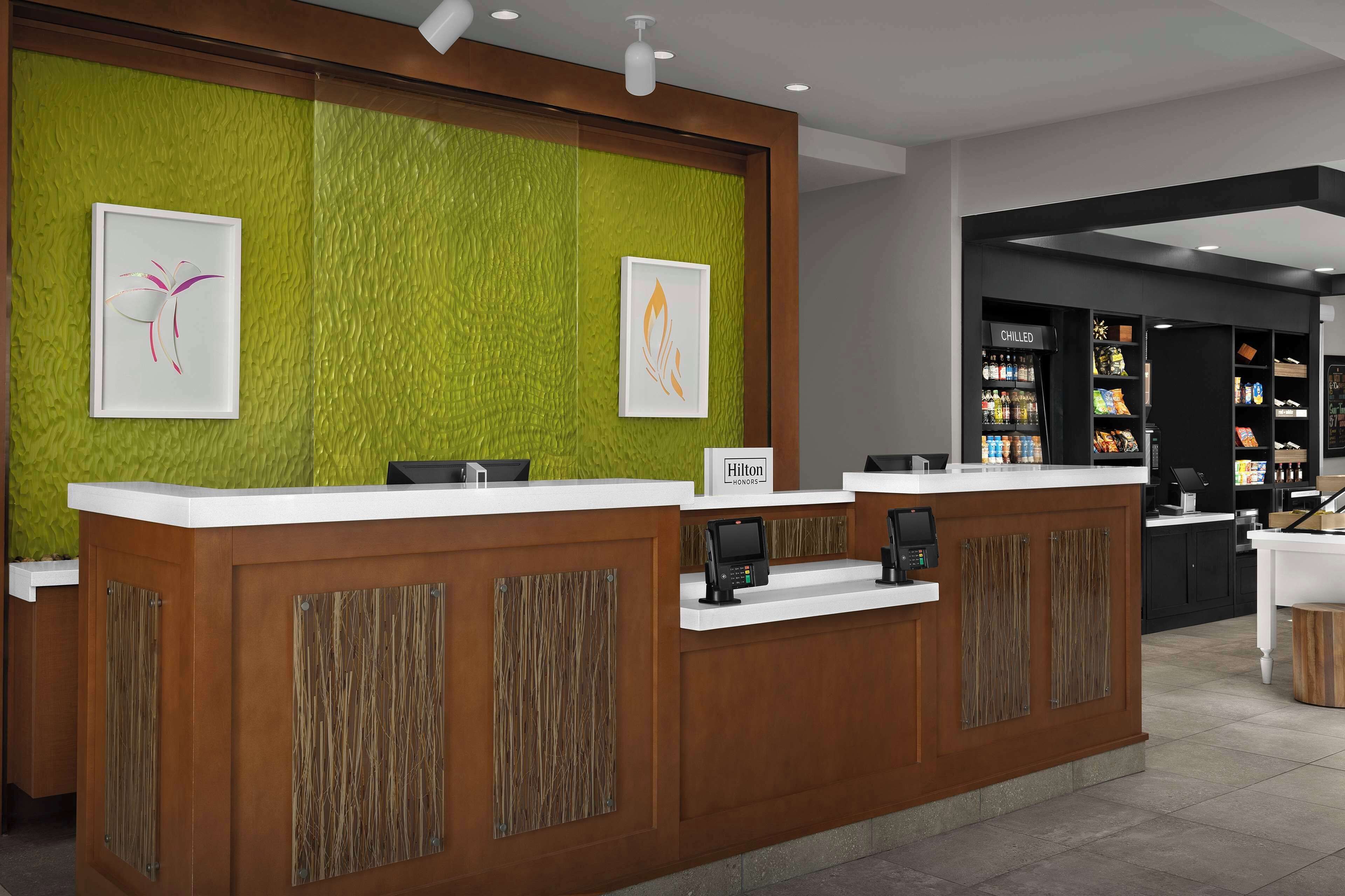 Uma receção de hotel com parede texturizada verde, obras de arte emolduradas e uma área de bar de pequenos-almoços.
