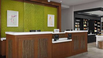 Uma receção de hotel com parede texturizada verde, obras de arte emolduradas e uma área de bar de pequenos-almoços.