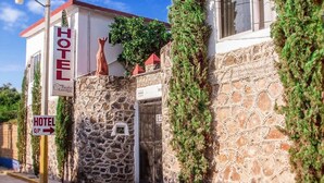 Um hotel com fachada de pedra, uma placa indicando hotel e uma área de estacionamento, além de uma escultura decorativa no telhado.