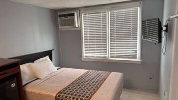 Quarto com cama, escrivaninha, ar condicionado e janela com persianas.
