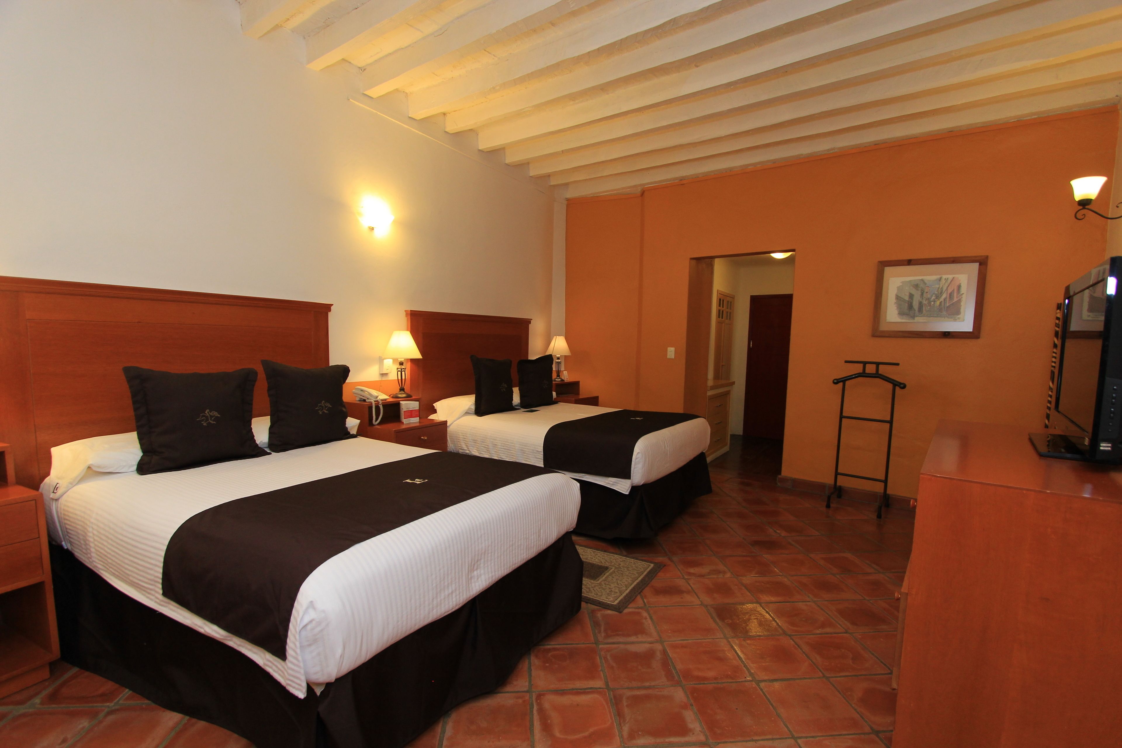 Quarto de hotel com duas camas, uma escrivaninha, uma cadeira e uma televisão.