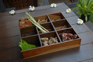 Uma bandeja de madeira com divisórias contendo diversas ervas e especiarias.