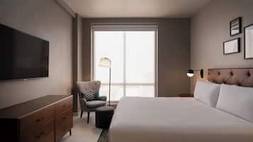 Quarto de hotel com cama grande, televisão de tela plana, cadeira, escrivaninha e janela com persianas.