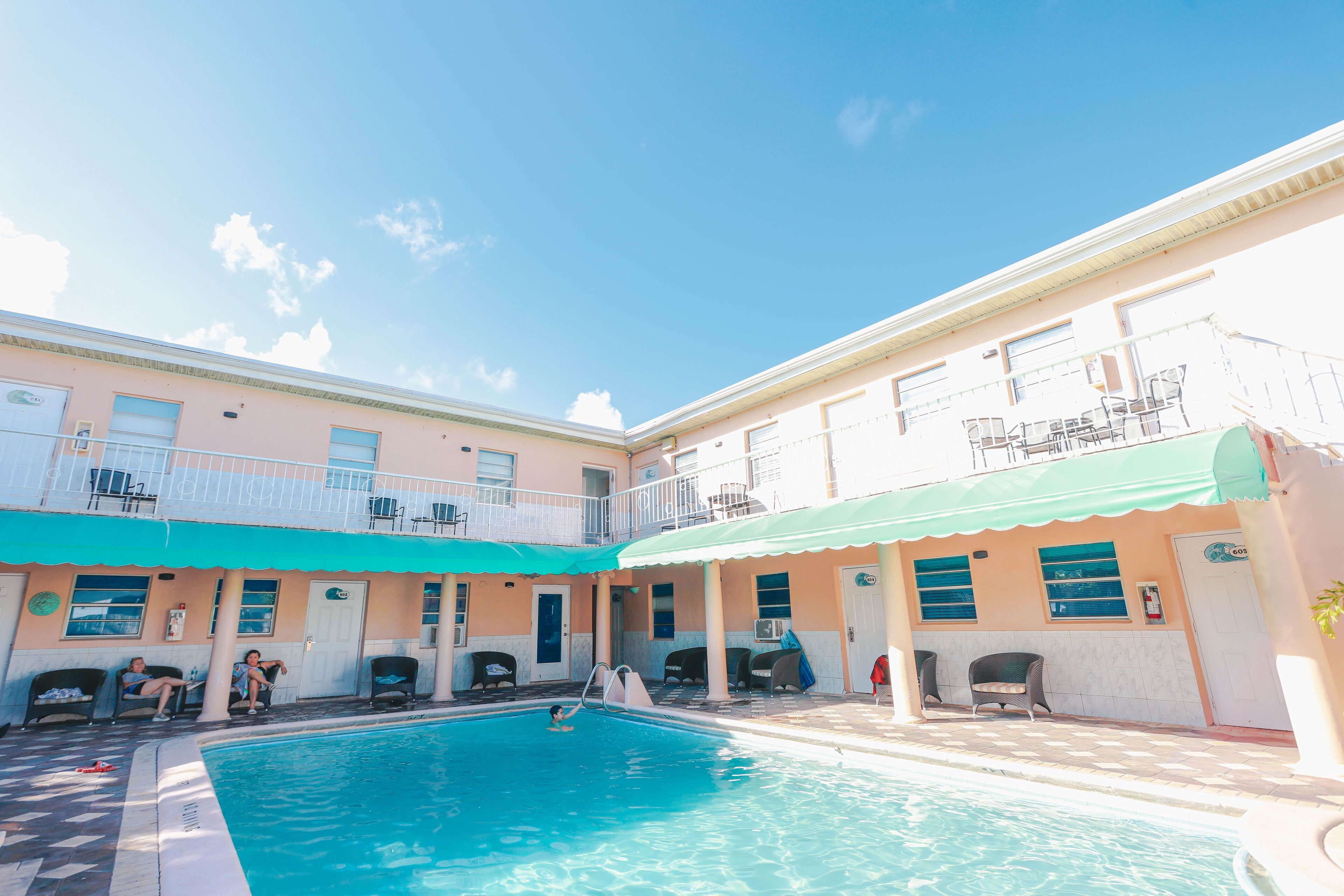 Uma área de piscina com espaço de estar coberto e um edifício com várias janelas e portas.