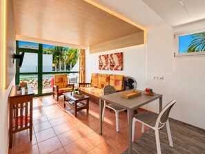 Uma sala de estar moderna com sofá, cadeiras, mesa de centro e mesa de jantar. Há uma janela com vista para palmeiras e um edifício.