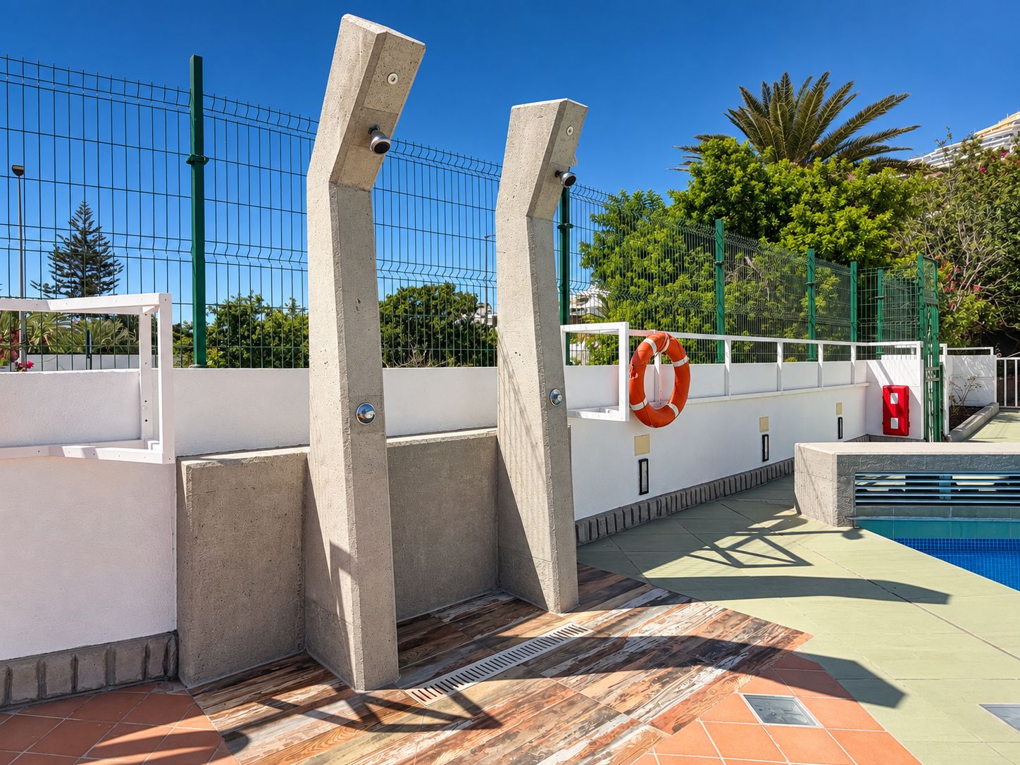 Área de piscina com barreira de concreto, boia salva-vidas e deck revestido com azulejos.