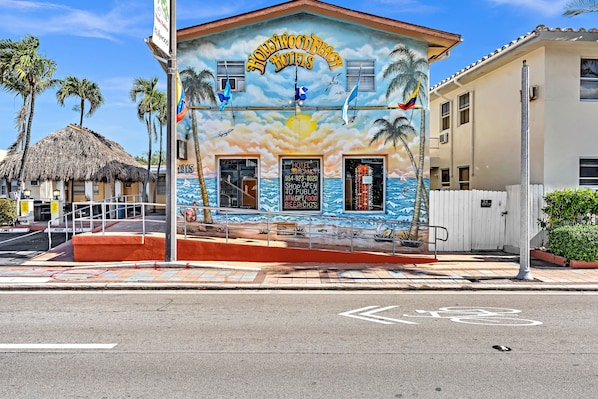 Um edifício com um mural de uma cena de praia, um letreiro para Hollywood Beach Hotels e um símbolo de ciclovia na rua.