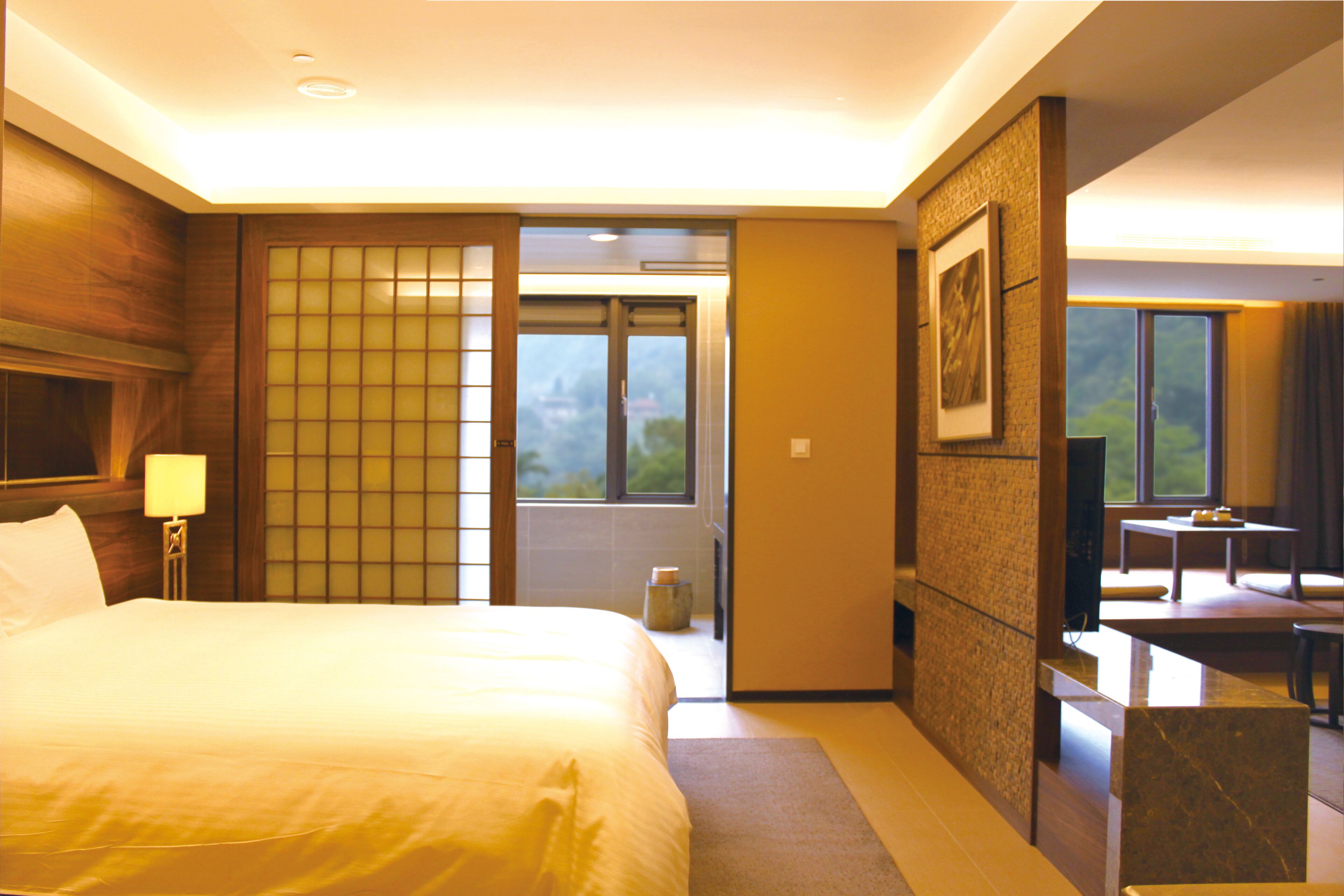 Quarto de hotel com uma cama grande, uma escrivaninha, uma cadeira e vista para o exterior através de uma janela.