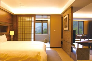 Quarto de hotel com uma cama grande, uma escrivaninha, uma cadeira e vista para o exterior através de uma janela.