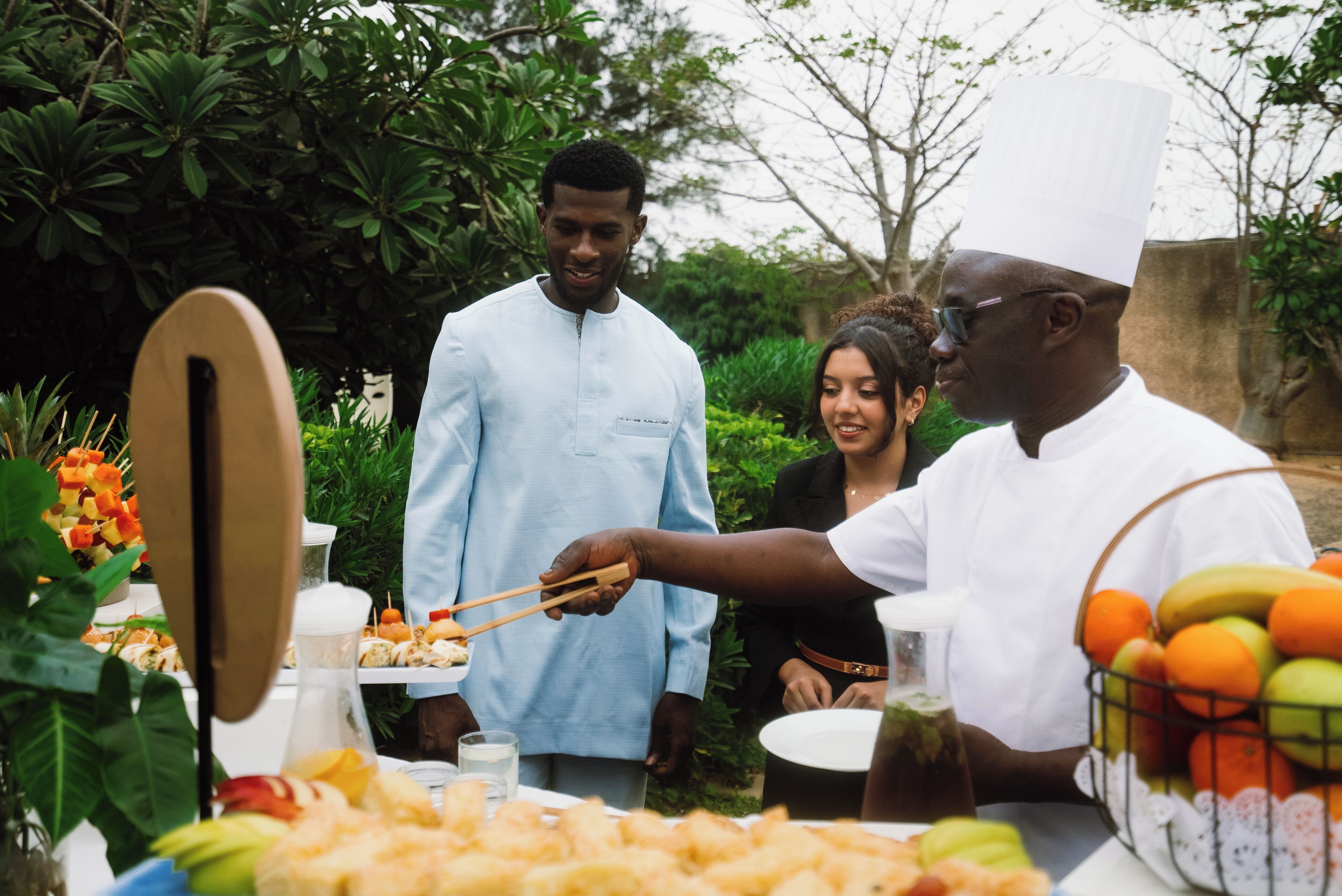 Disposição de buffet com diversos alimentos e uma pessoa servindo comida com hashis.