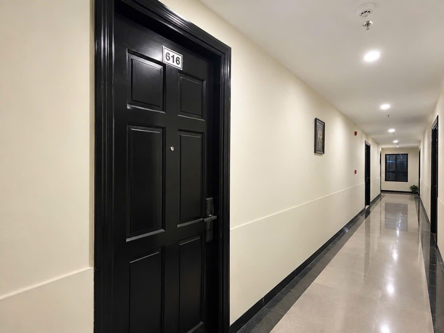 Corredor com porta preta identificada com o número 616, dando acesso a um quarto.