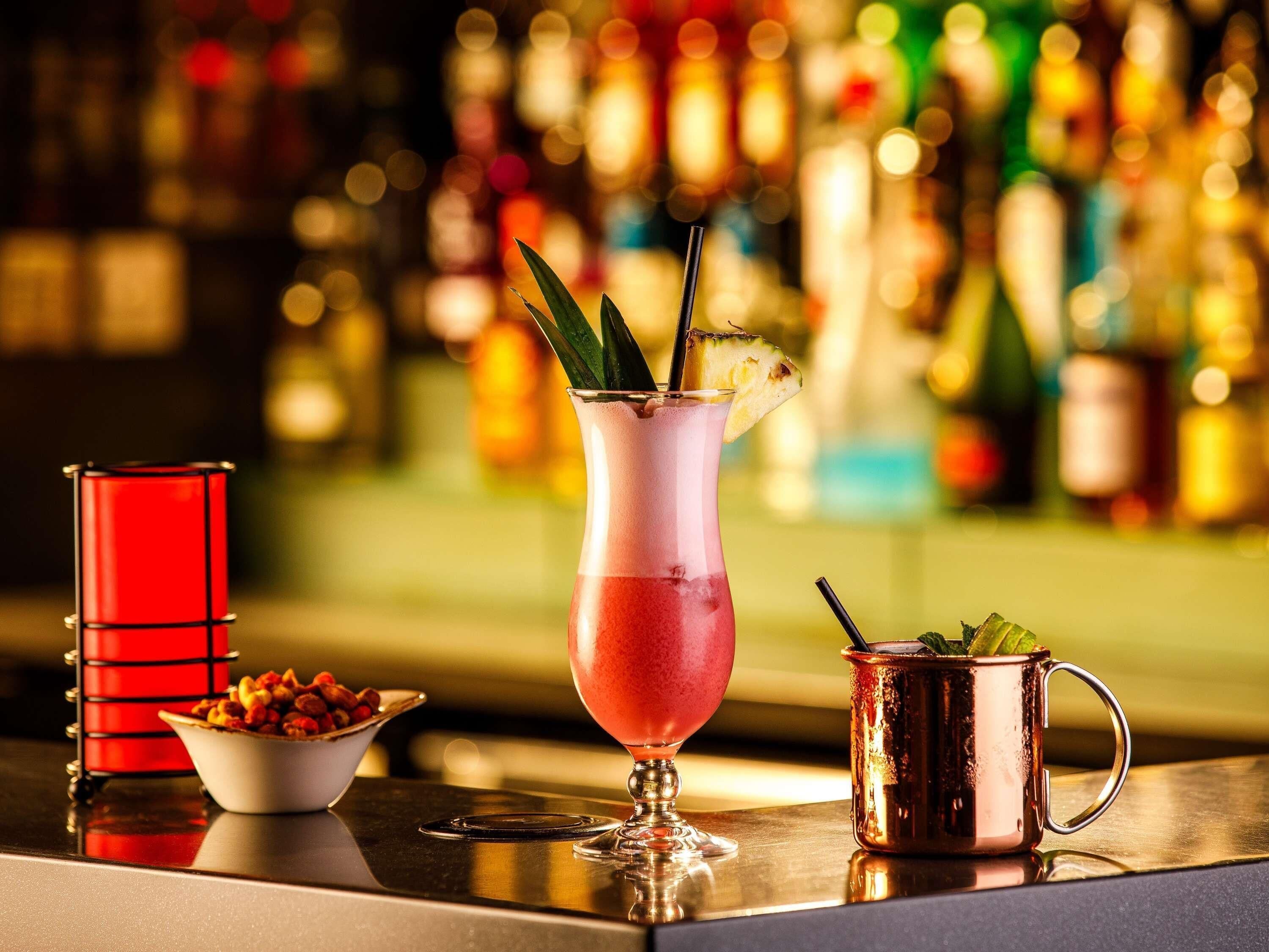 Um bar com um coquetel num copo, uma bebida vermelha num copo e um caneco de cobre.