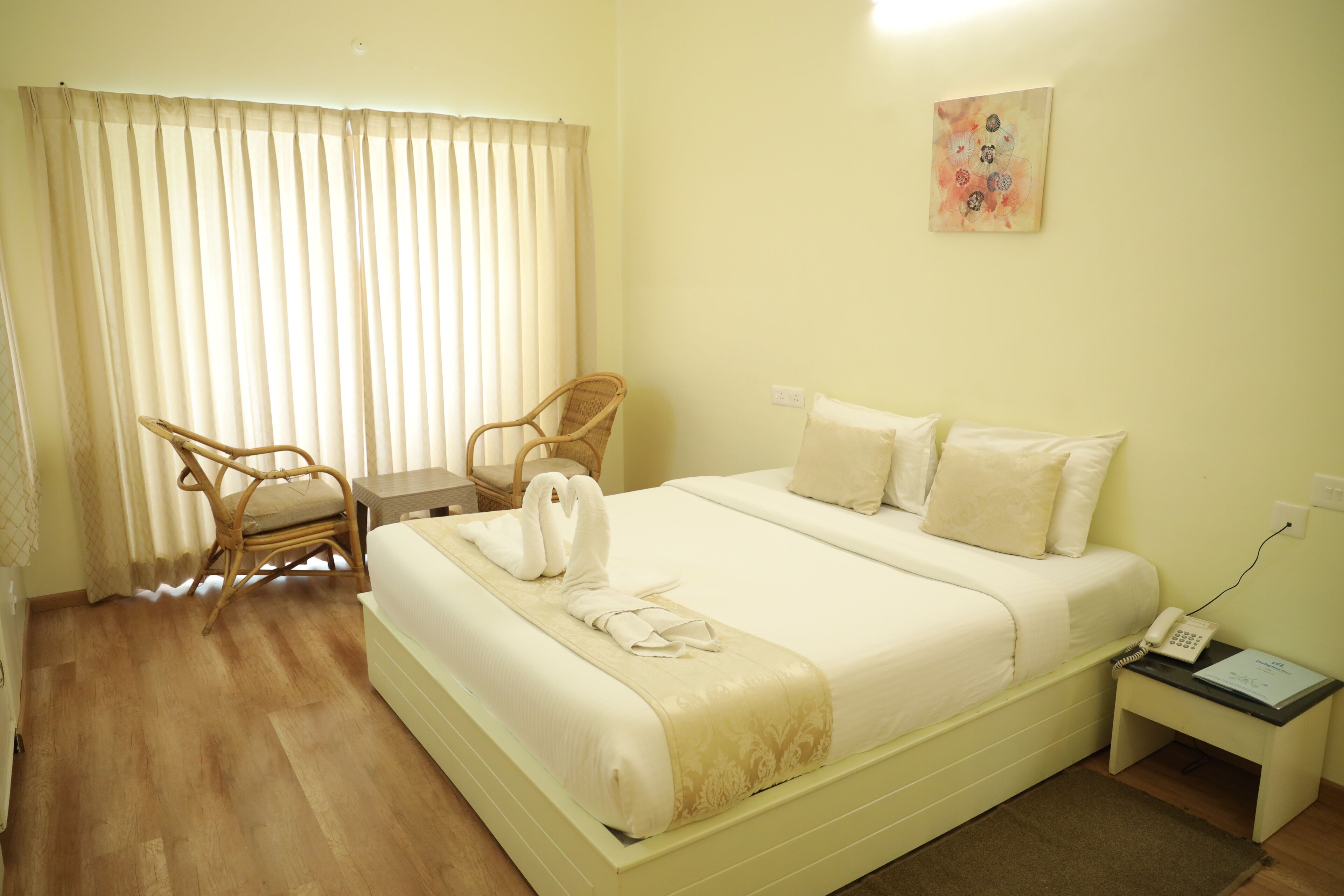 Quarto de hotel com cama, duas cadeiras, mesa de cabeceira, telefone e um quadro na parede.