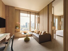 Quarto de hotel moderno com uma grande janela com vista para a cidade, um sofá, uma mesa de jantar e uma televisão.