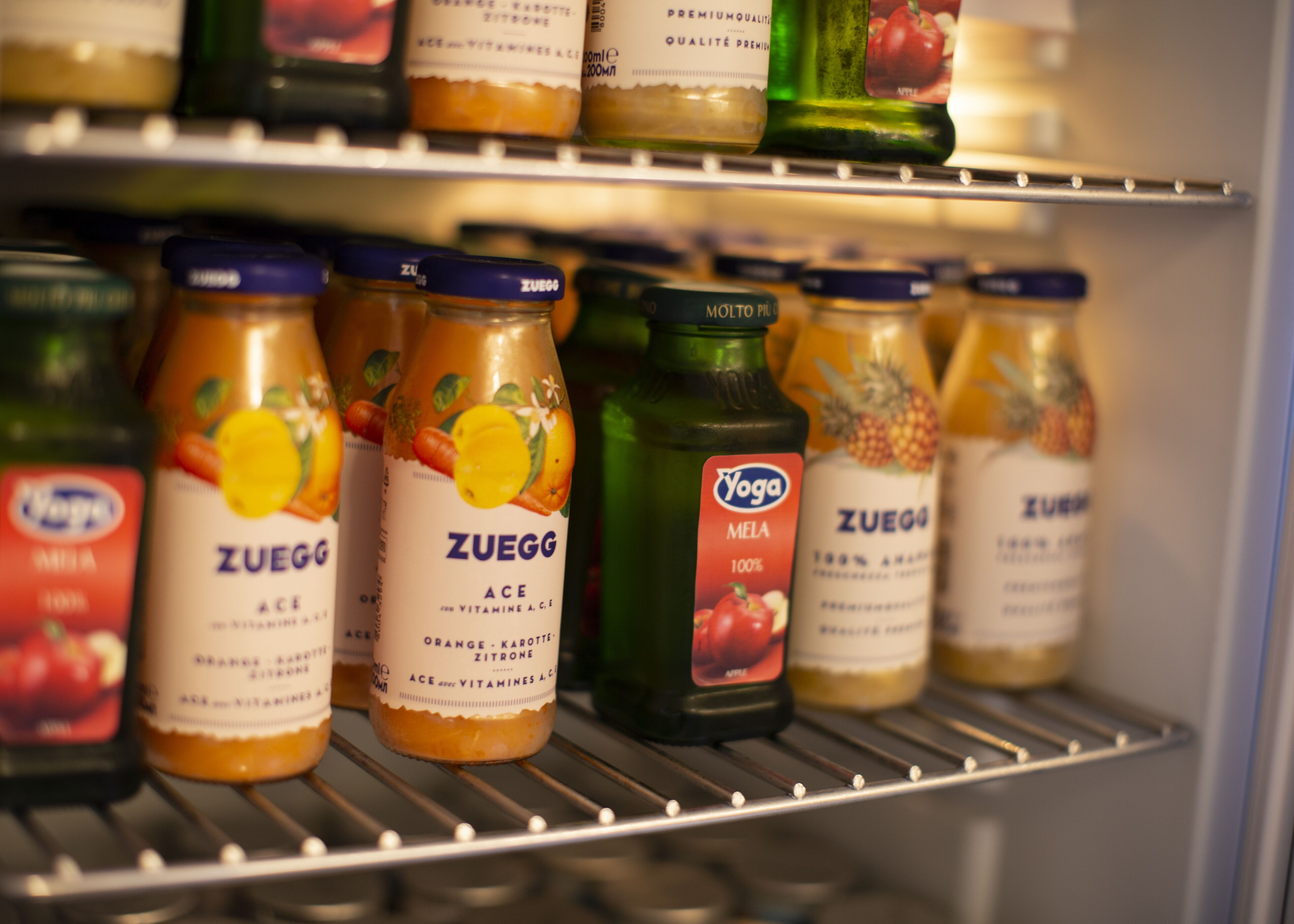 Prateleira refrigerada com diversos alimentos, incluindo potes com as etiquetas 'Zuegg' e 'Yoga'.
