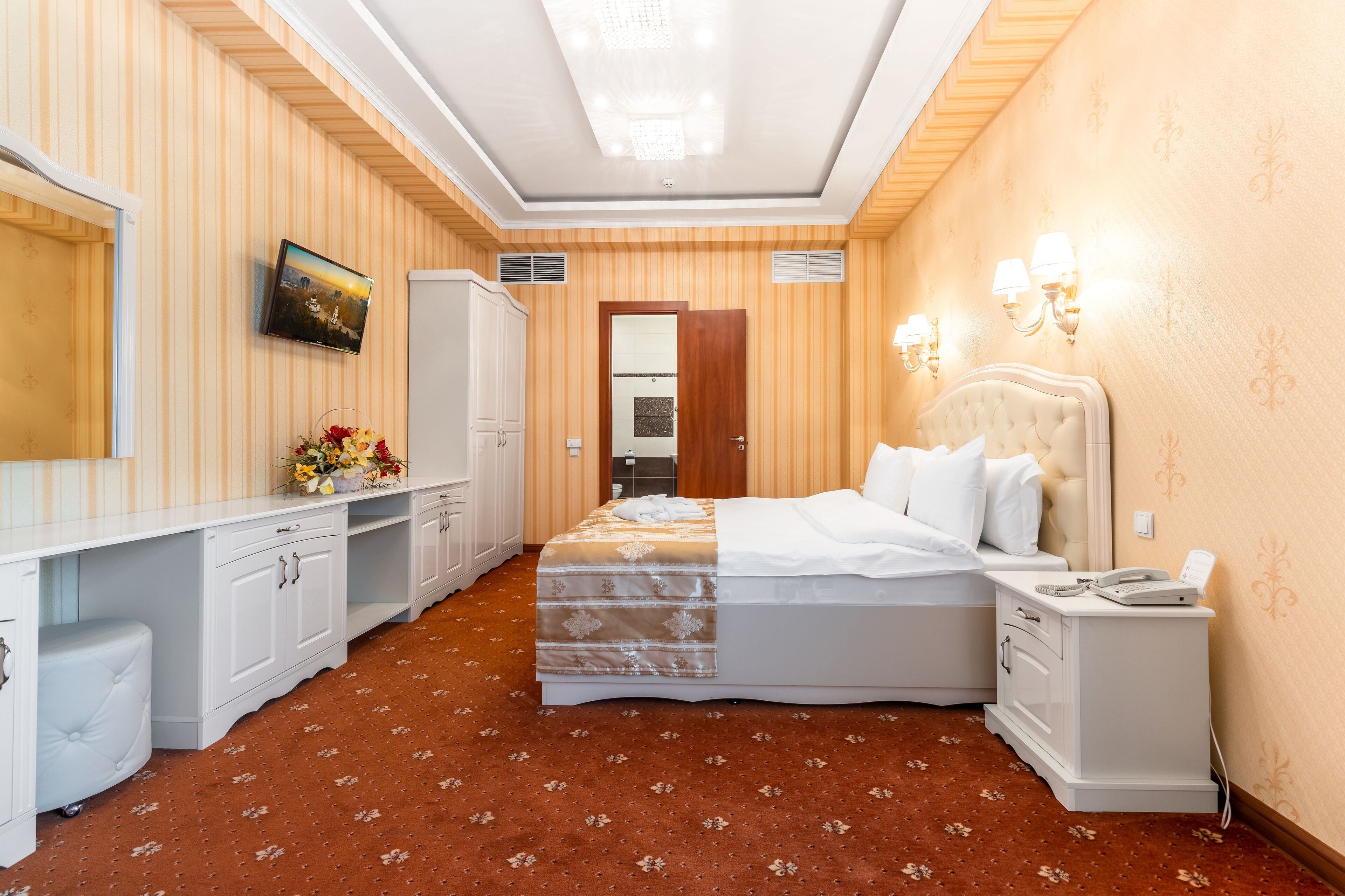 Quarto de hotel com cama, mesa de cabeceira, abajur e televisão na parede.