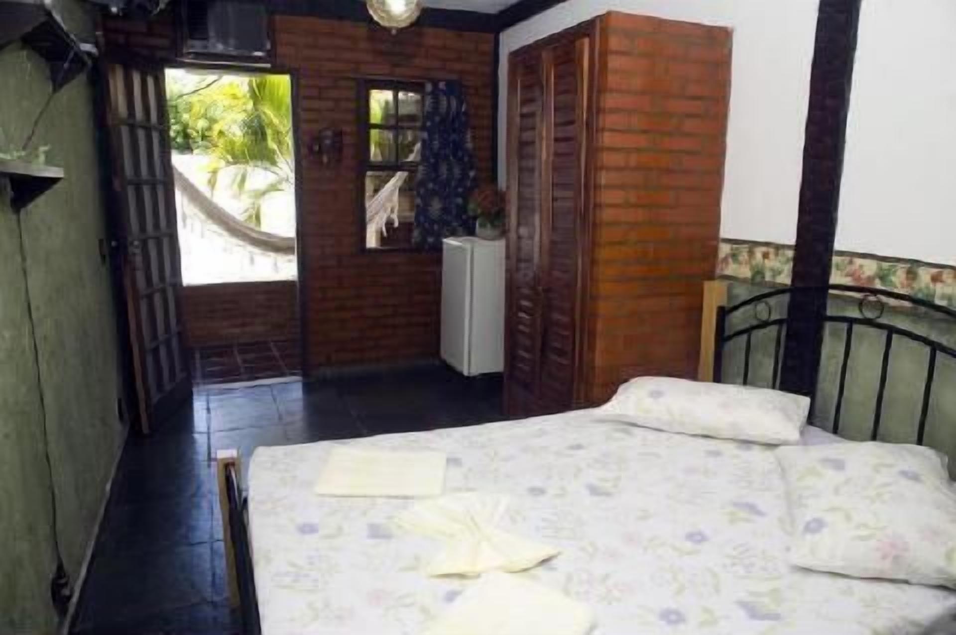 Um quarto com uma cama, um guarda-roupa de madeira, um frigorífico branco pequeno e uma rede.
