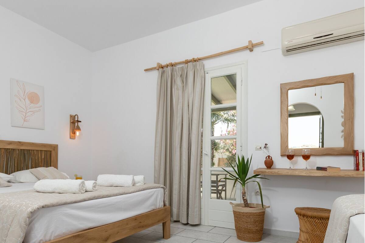 Quarto com cama de madeira, planta em vaso, espelho e vista para o exterior.