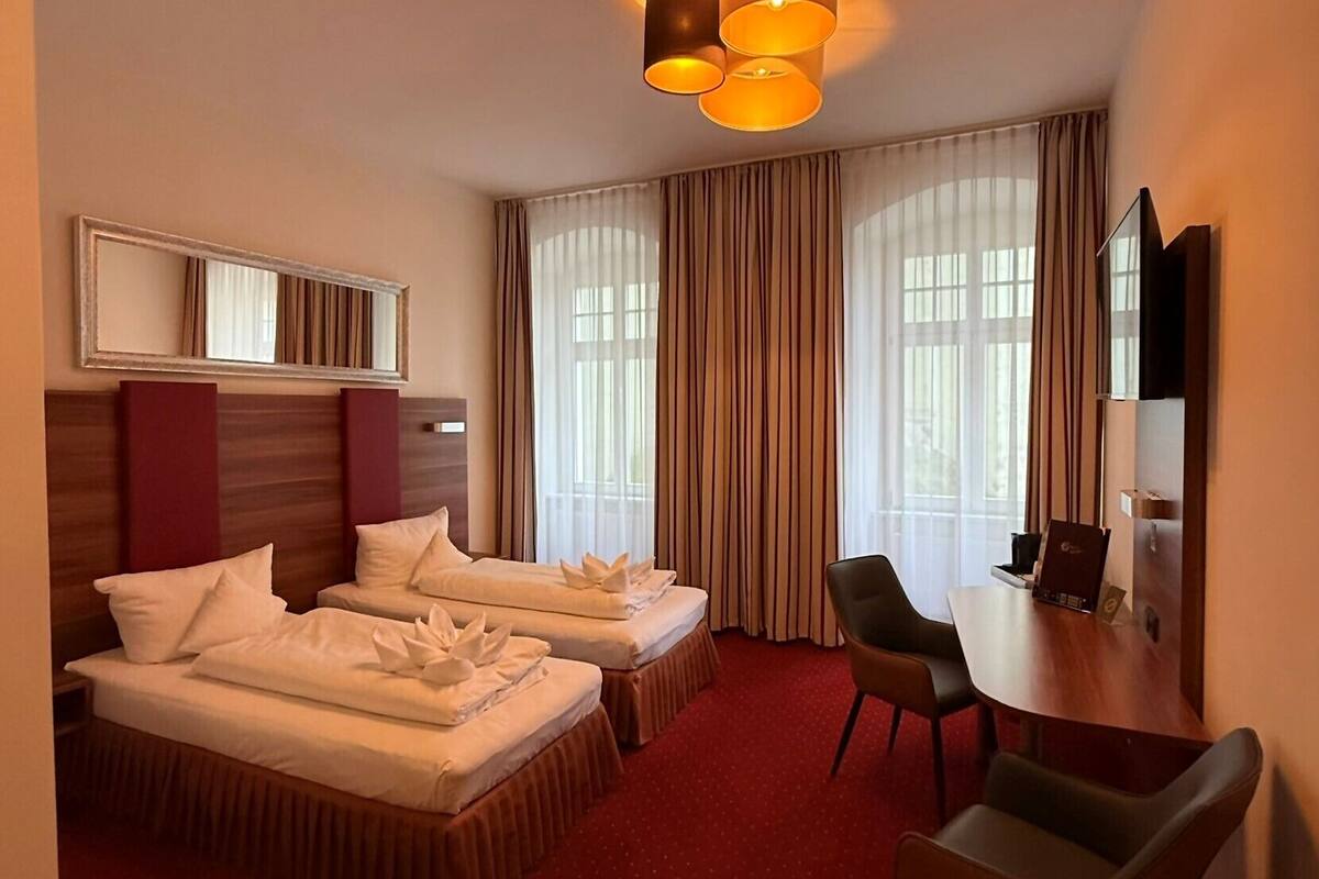 Quarto de hotel com duas camas, uma escrivaninha, uma cadeira e um espelho grande.