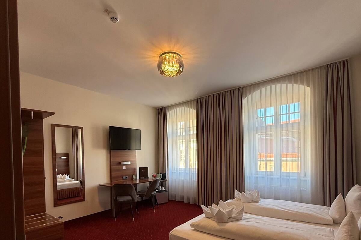 Quarto de hotel com uma cama grande, uma escrivaninha com cadeira, uma televisão e um espelho.