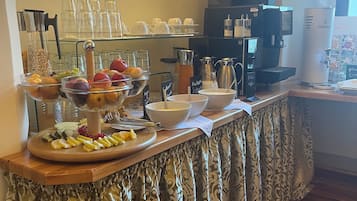Disposição de buffet com diversos alimentos e bebidas, incluindo uma máquina de café e copos.