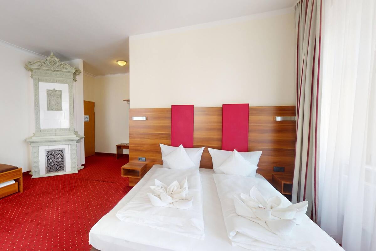 Quarto de hotel com cama, sofá, lareira e tapete vermelho.