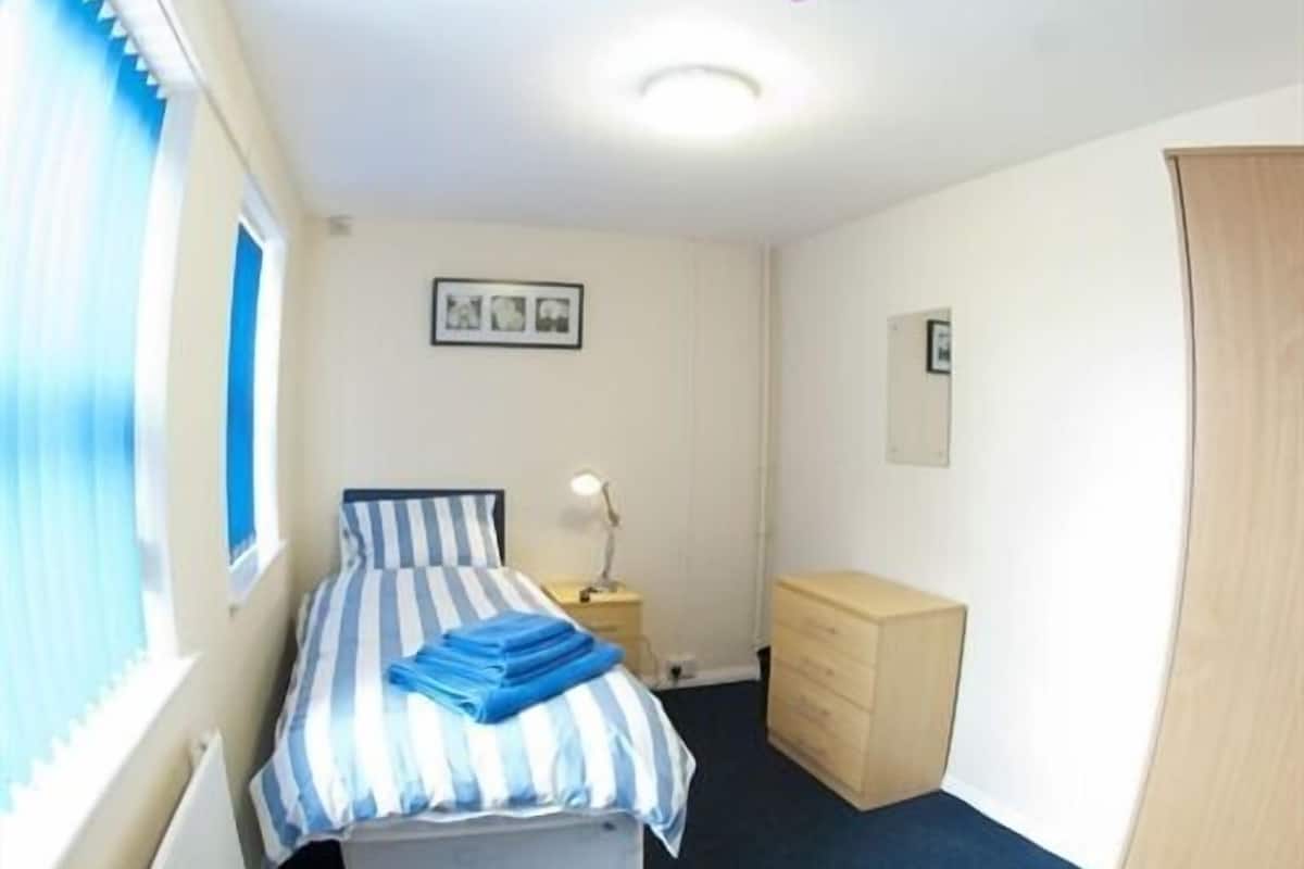 Quarto com cama, penteadeira, mesa de cabeceira e janela com persianas.