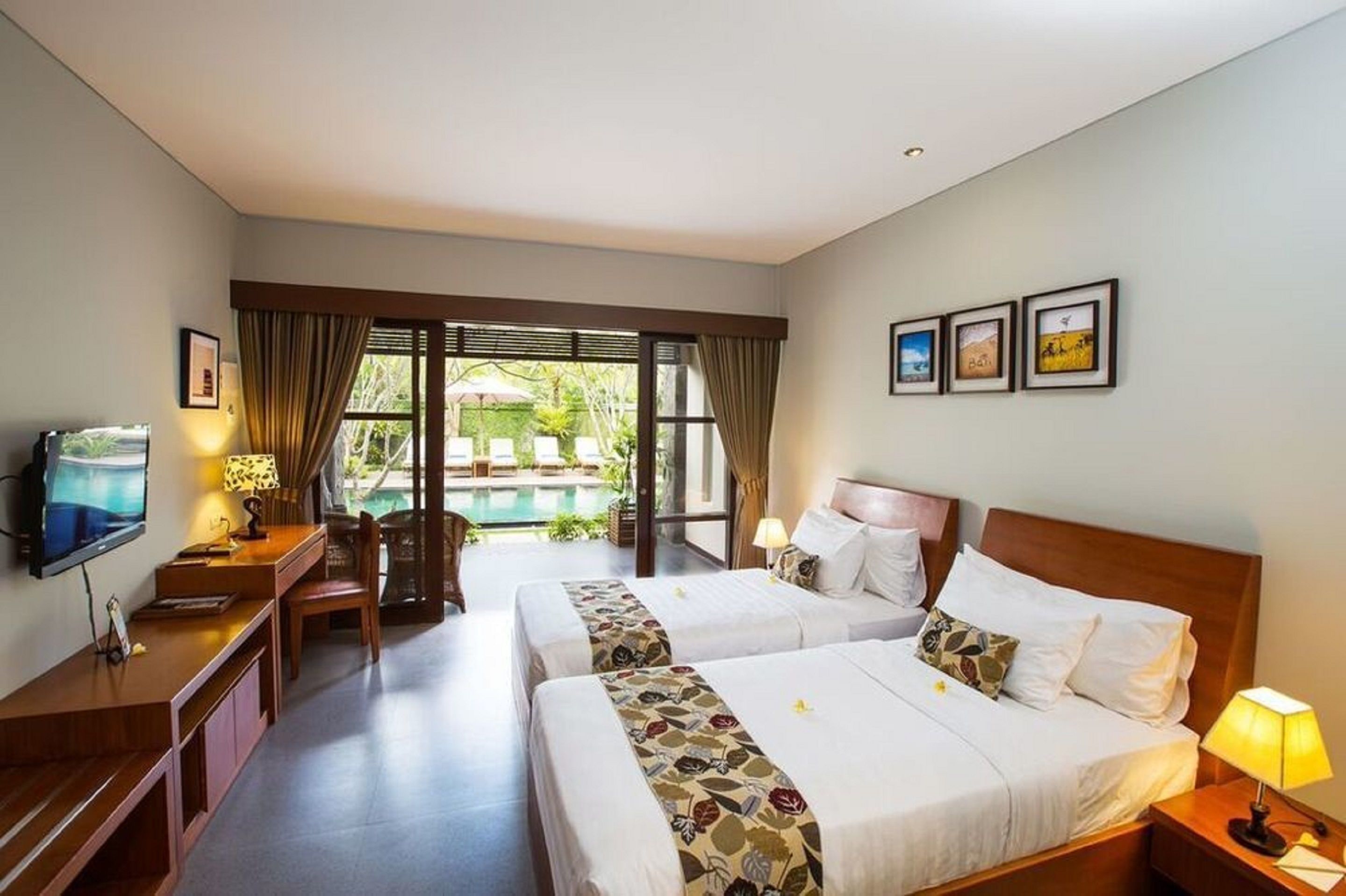 Quarto de hotel com duas camas, uma escrivaninha, televisão e vista para a piscina.