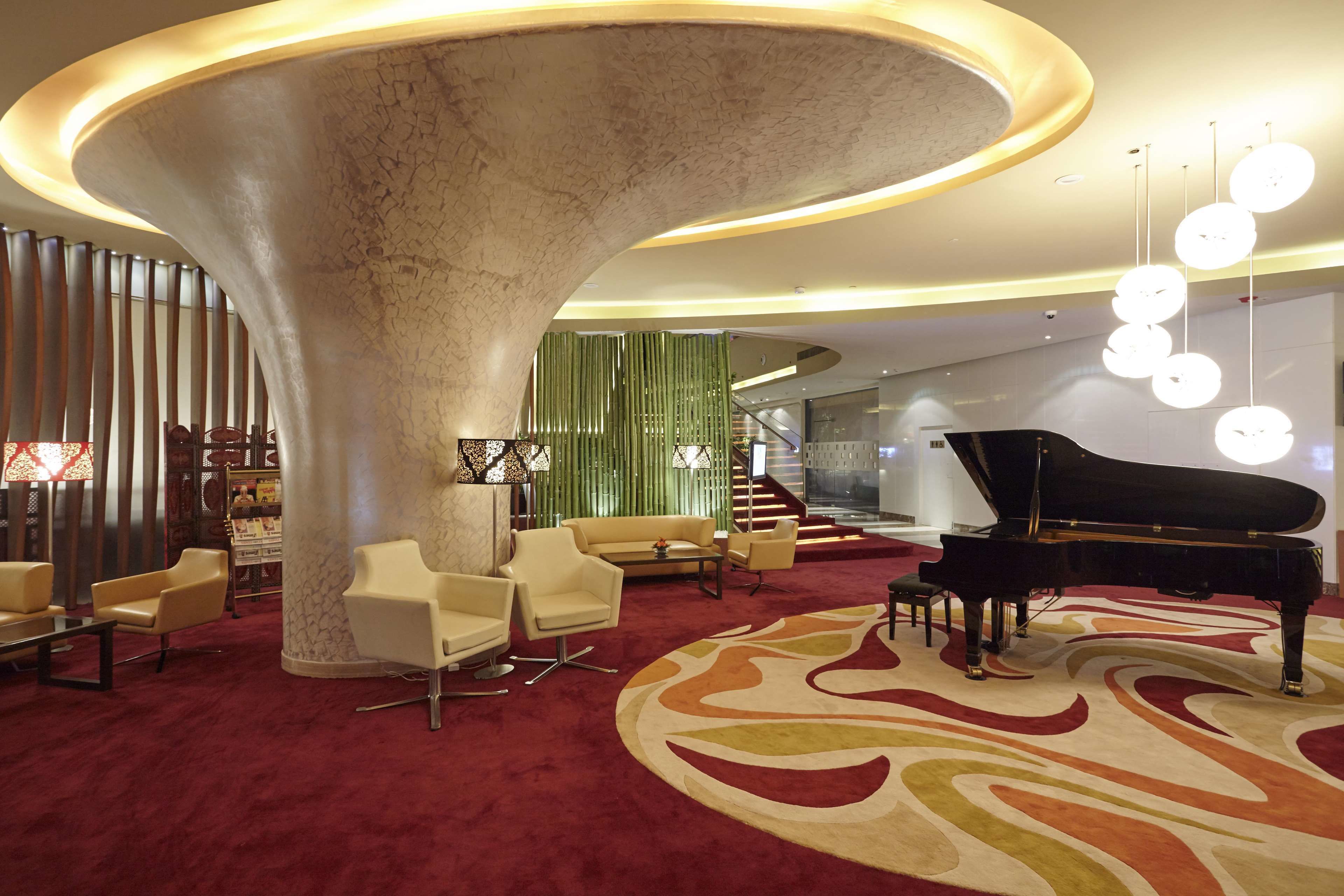 Um hall amplo com um piano de cauda, assentos confortáveis e um imponente pilar circular.