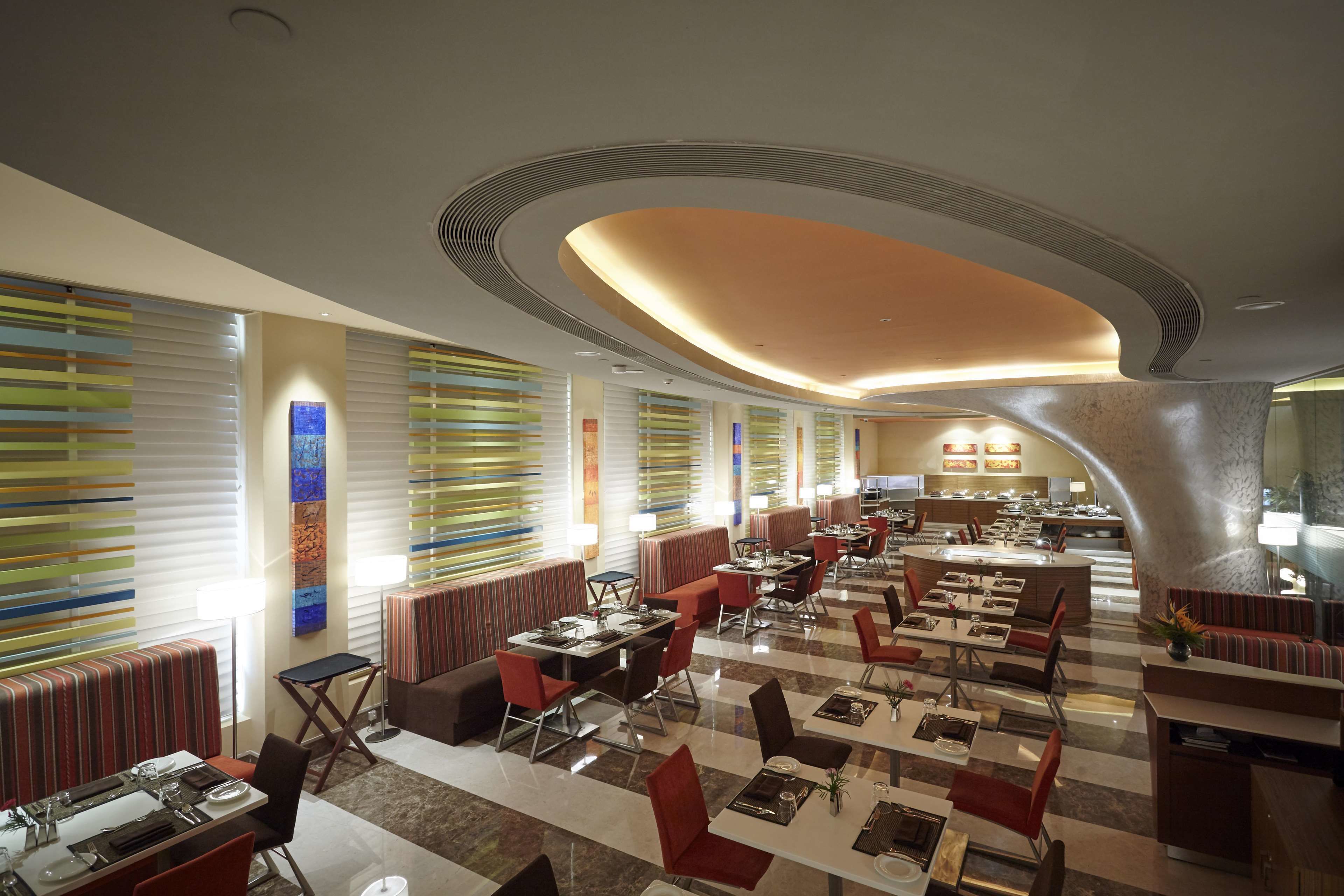 Um restaurante moderno com várias áreas de refeição, incluindo cabines e mesas, e uma área central com teto curvo.