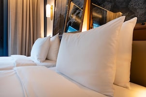 Quarto de hotel com cama, almofadas, cabeceira, cortinas e parede com textura.