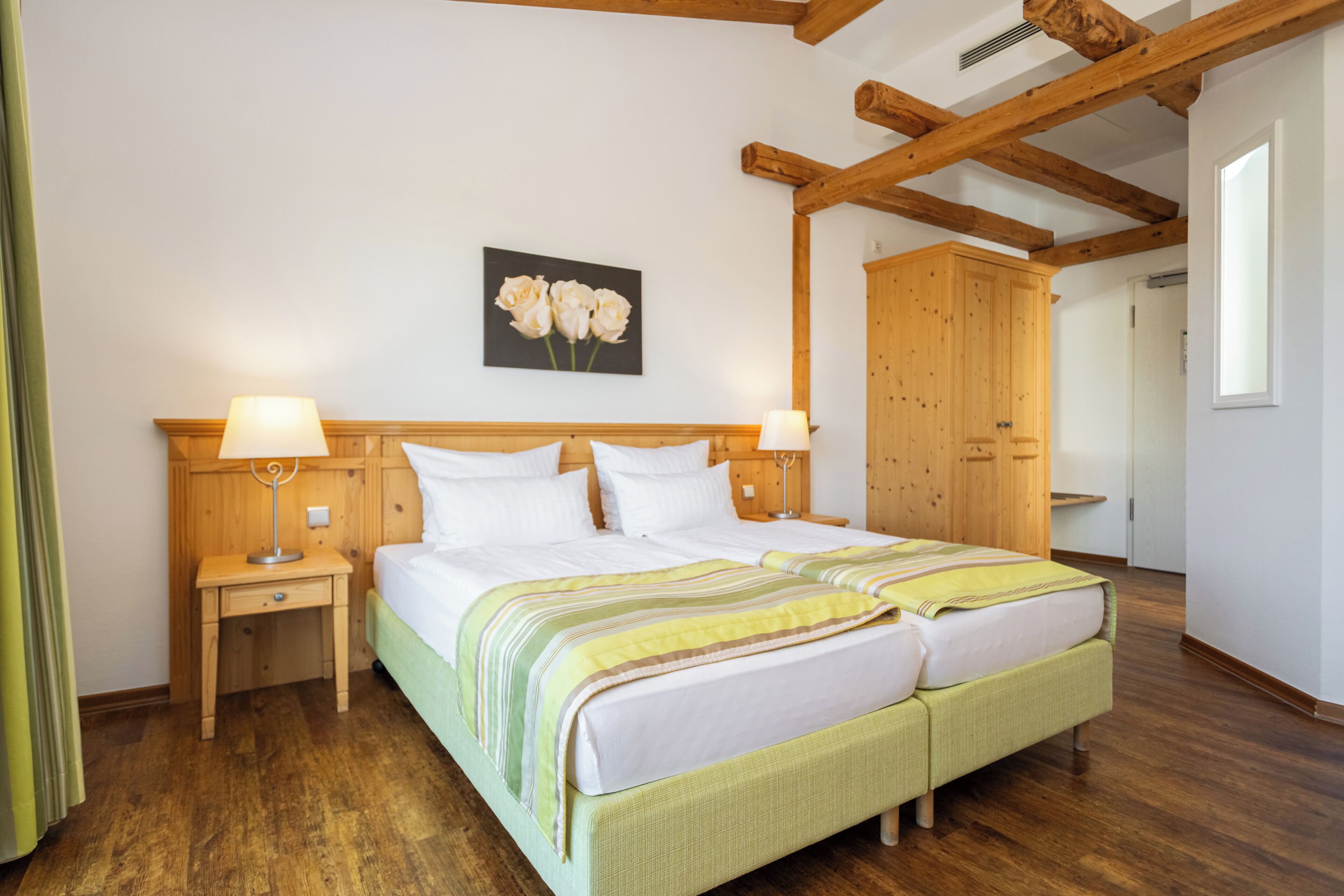 Uma cama de casal com manta listrada, cabeceira de madeira, mesas de cabeceira com abajures e um guarda-roupa de madeira.