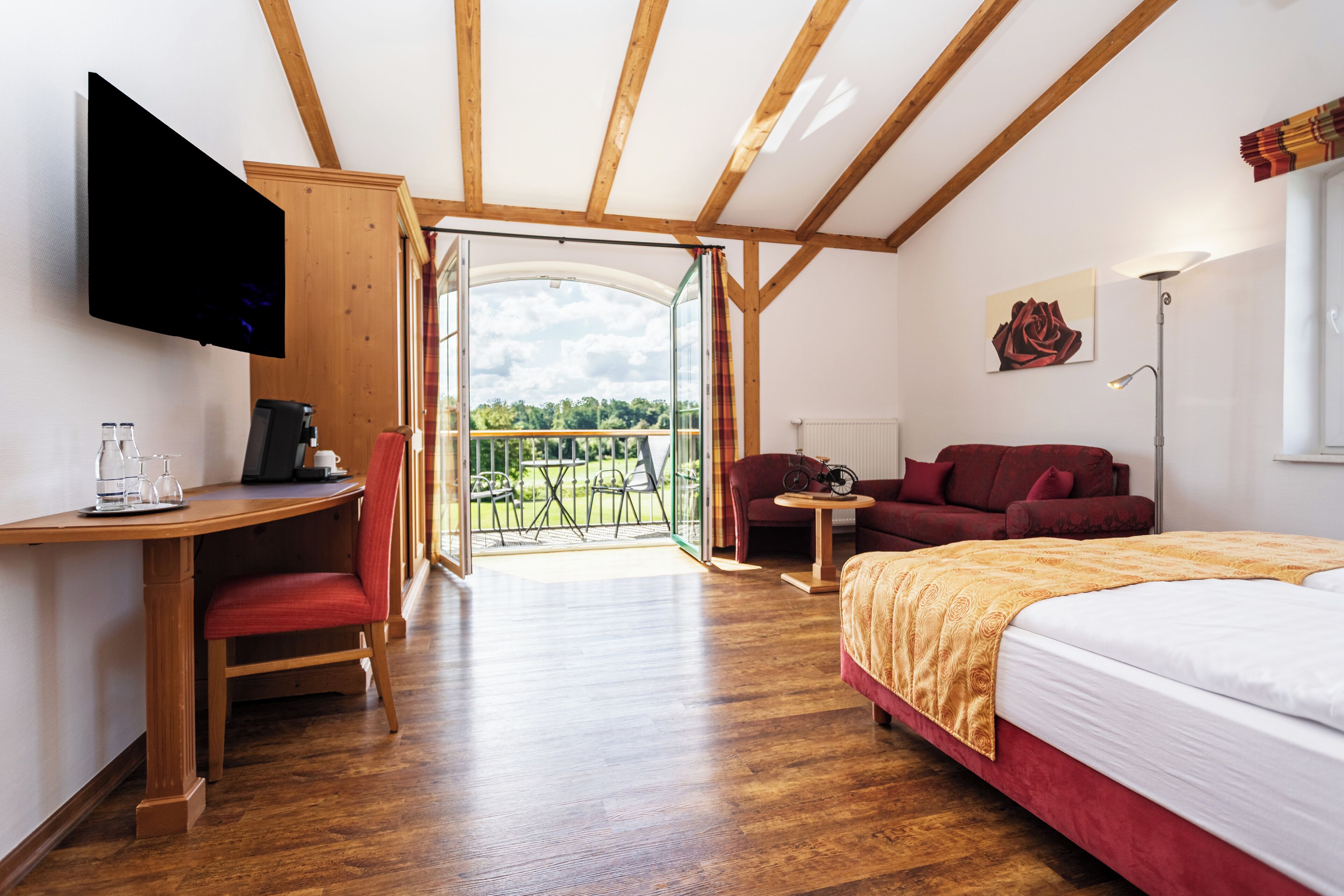 Quarto com cama, escrivaninha com cadeira, sofá e televisão. Possui varanda com vista para o verde.