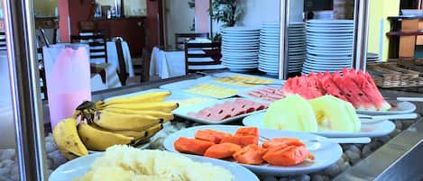 Buffet com diversas frutas e vegetais, incluindo bananas, melancia e cenouras, dispostos em pratos.