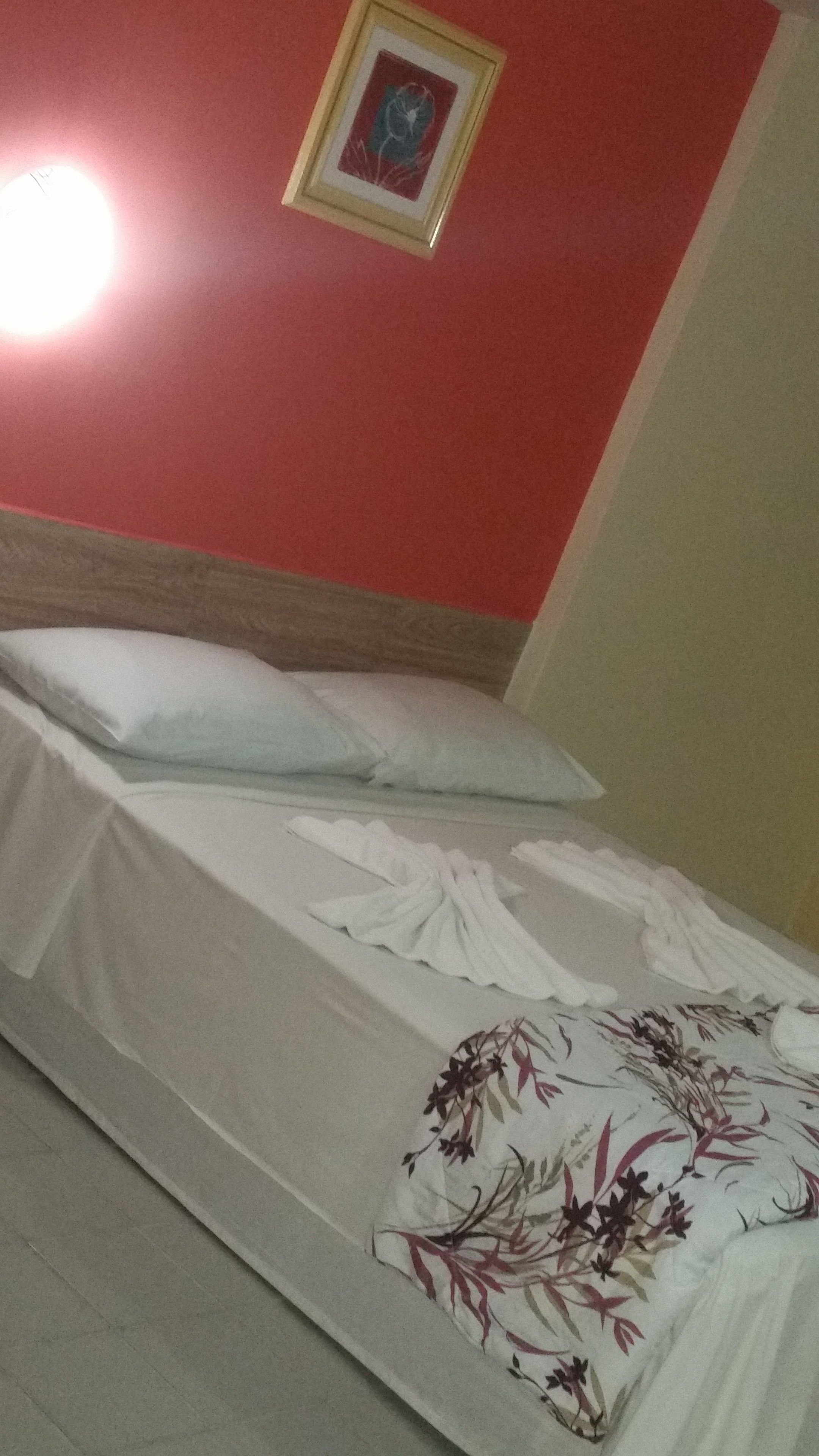 Uma cama com roupa de cama branca e um cobertor estampado com flores, um travesseiro branco e um quadro na parede.