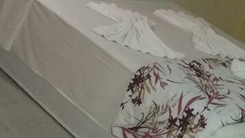 Uma cama com roupa de cama branca e um cobertor estampado com flores, um travesseiro branco e um quadro na parede.