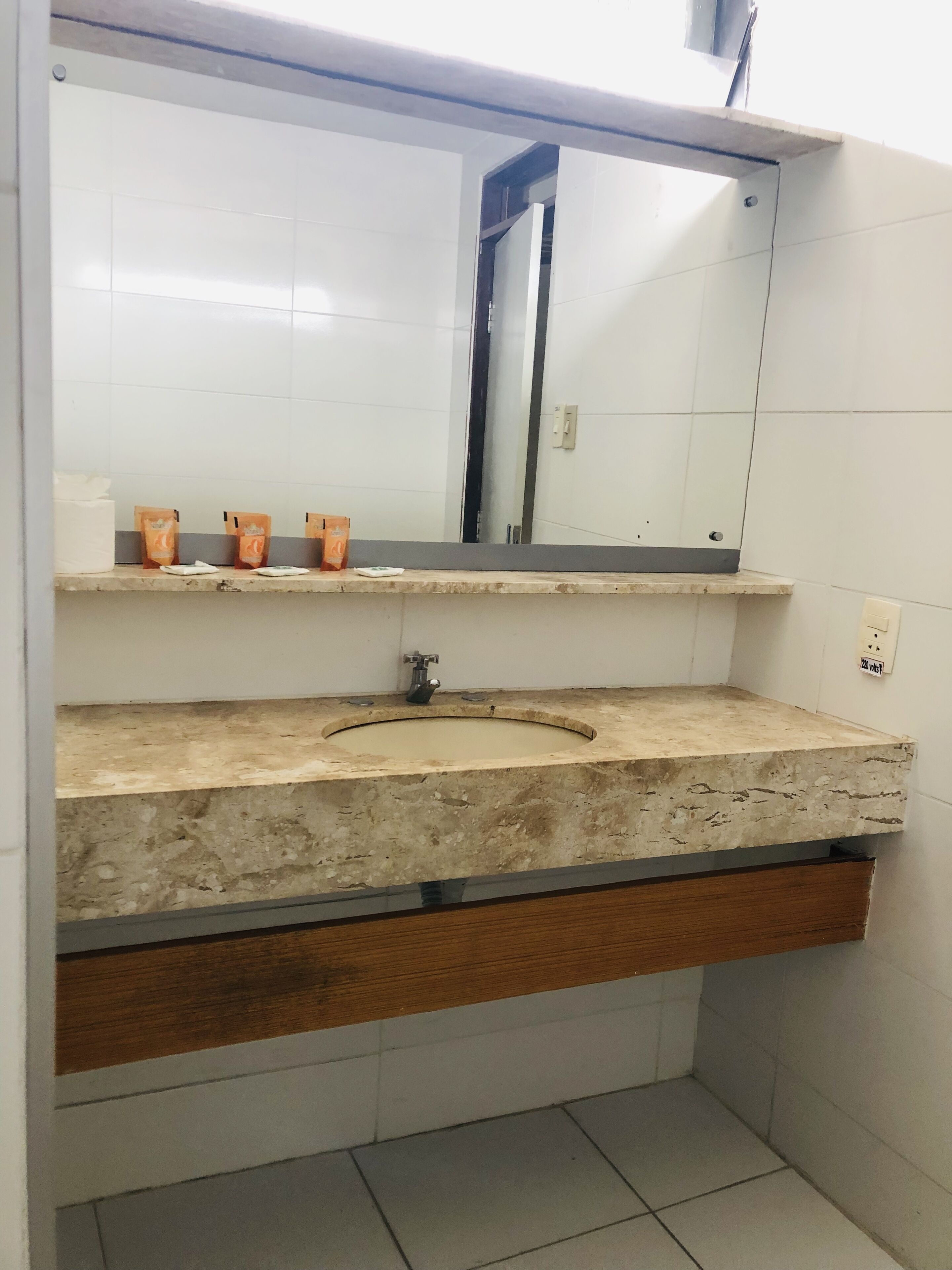 Casa de banho com um espelho grande, uma pia e uma prateleira com produtos de higiene pessoal.