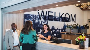 Uma receção com um letreiro 'WELCOME', um design de interiores moderno e vista para a cidade através da janela.